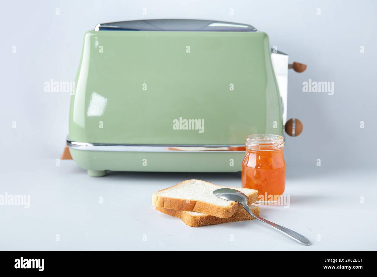 Toaster with tasty toast, jar of apricot jam and spoon on white ...