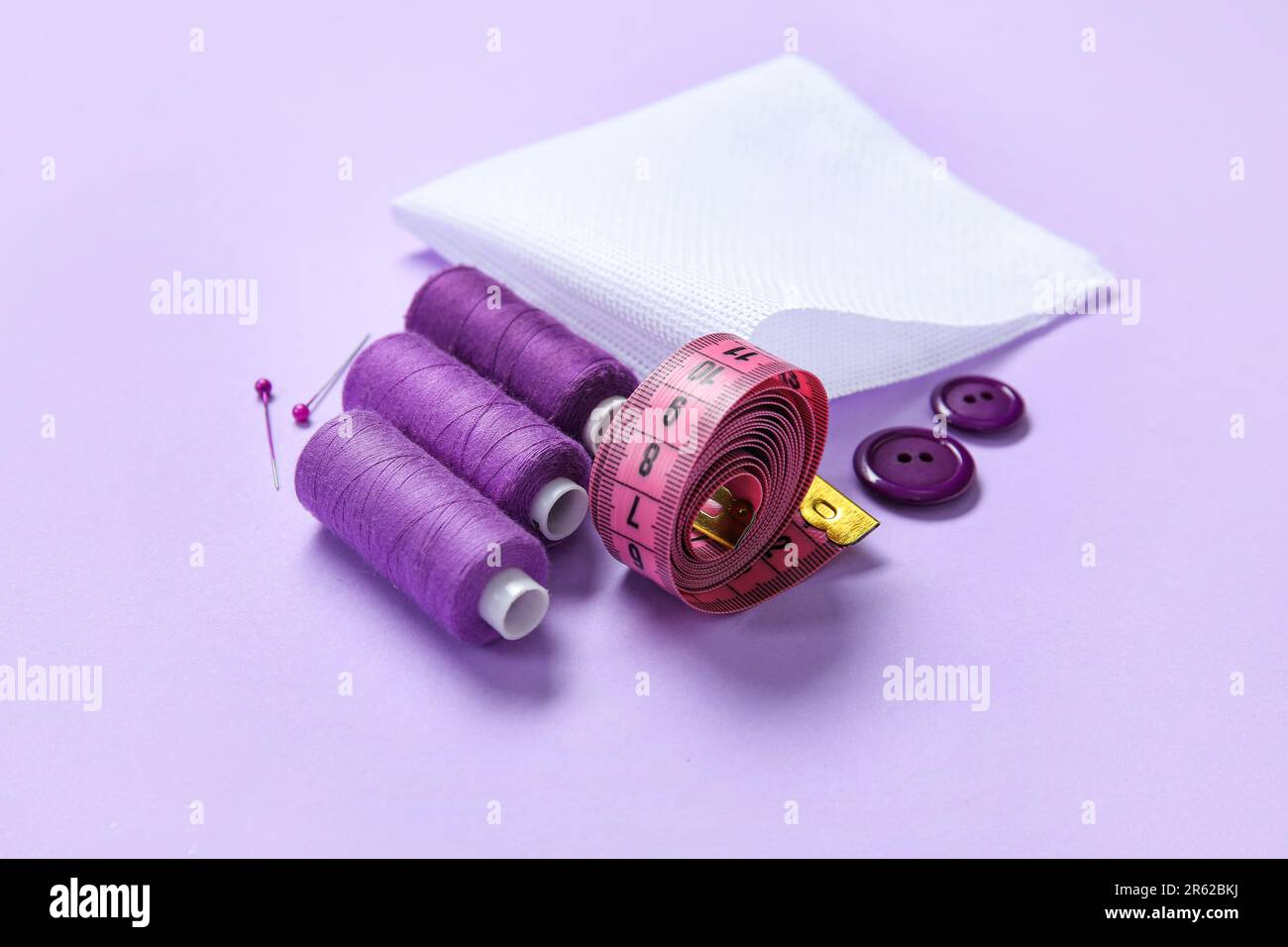 Canvas with buttons, thread spools and measuring tape on lilac ...