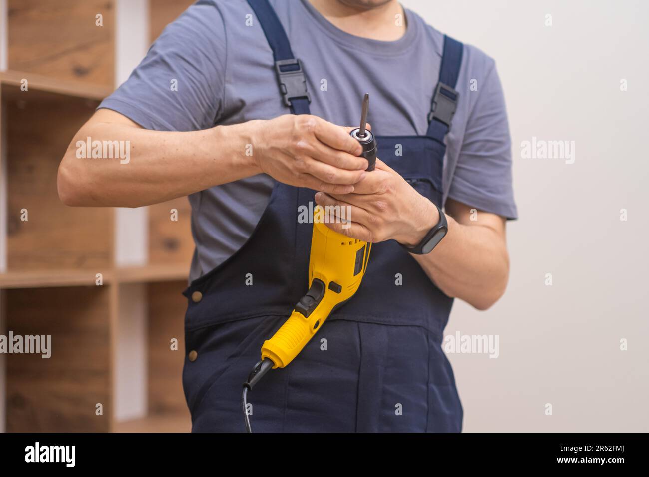 Skilled furniture technician in uniform using an electrical screwdriver ...