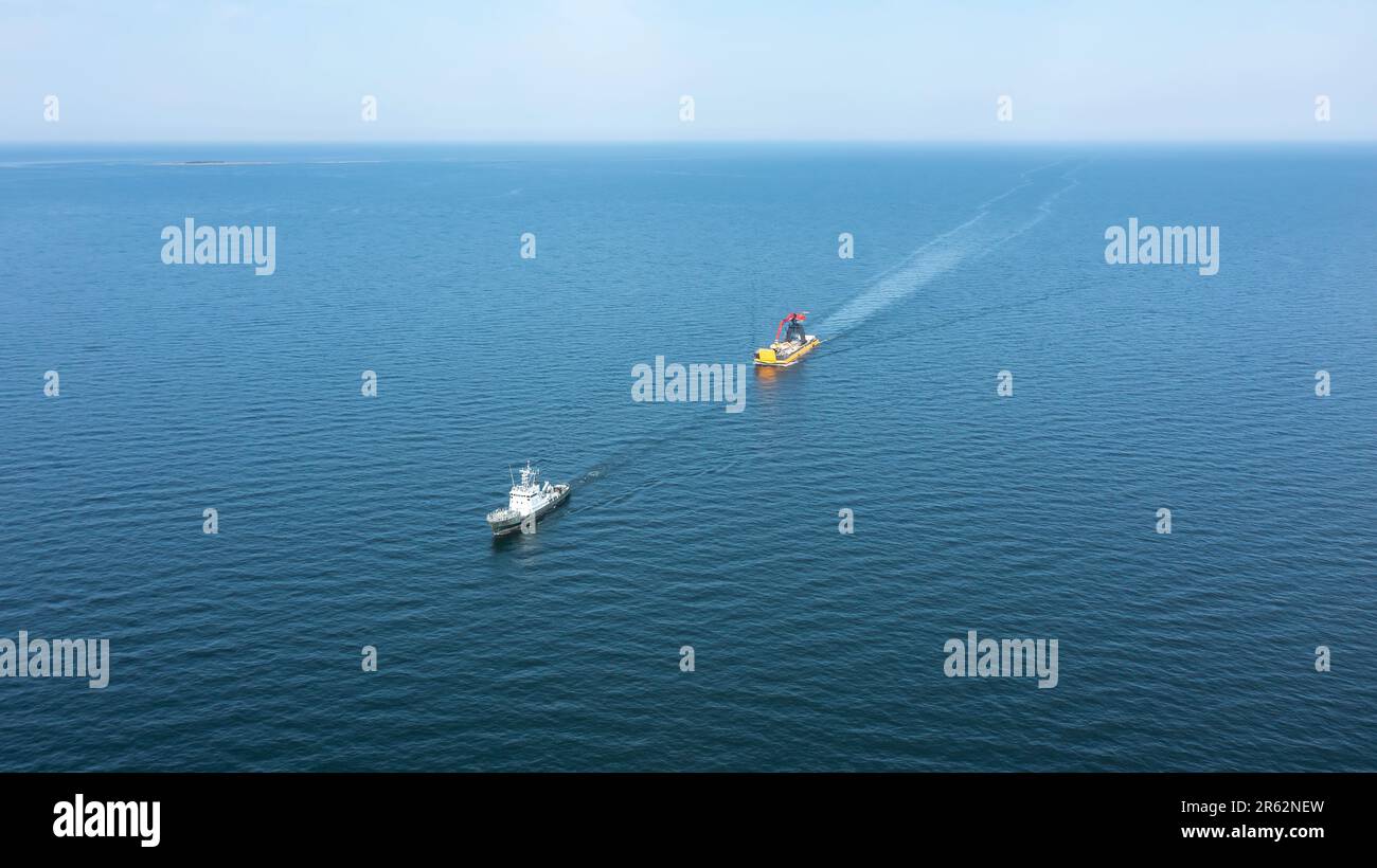 Tug boat travelling across the open ocean pulling a yellow barge loaded ...