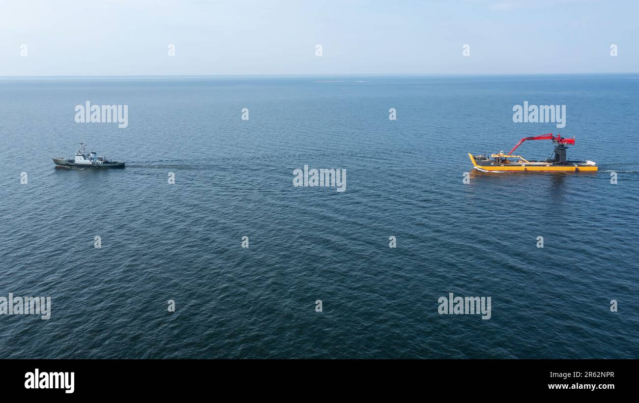Tug boat travelling across open ocean pulling a yellow barge loaded ...