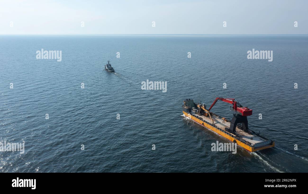 Tug boat travelling across open ocean pulling a yellow barge loaded ...