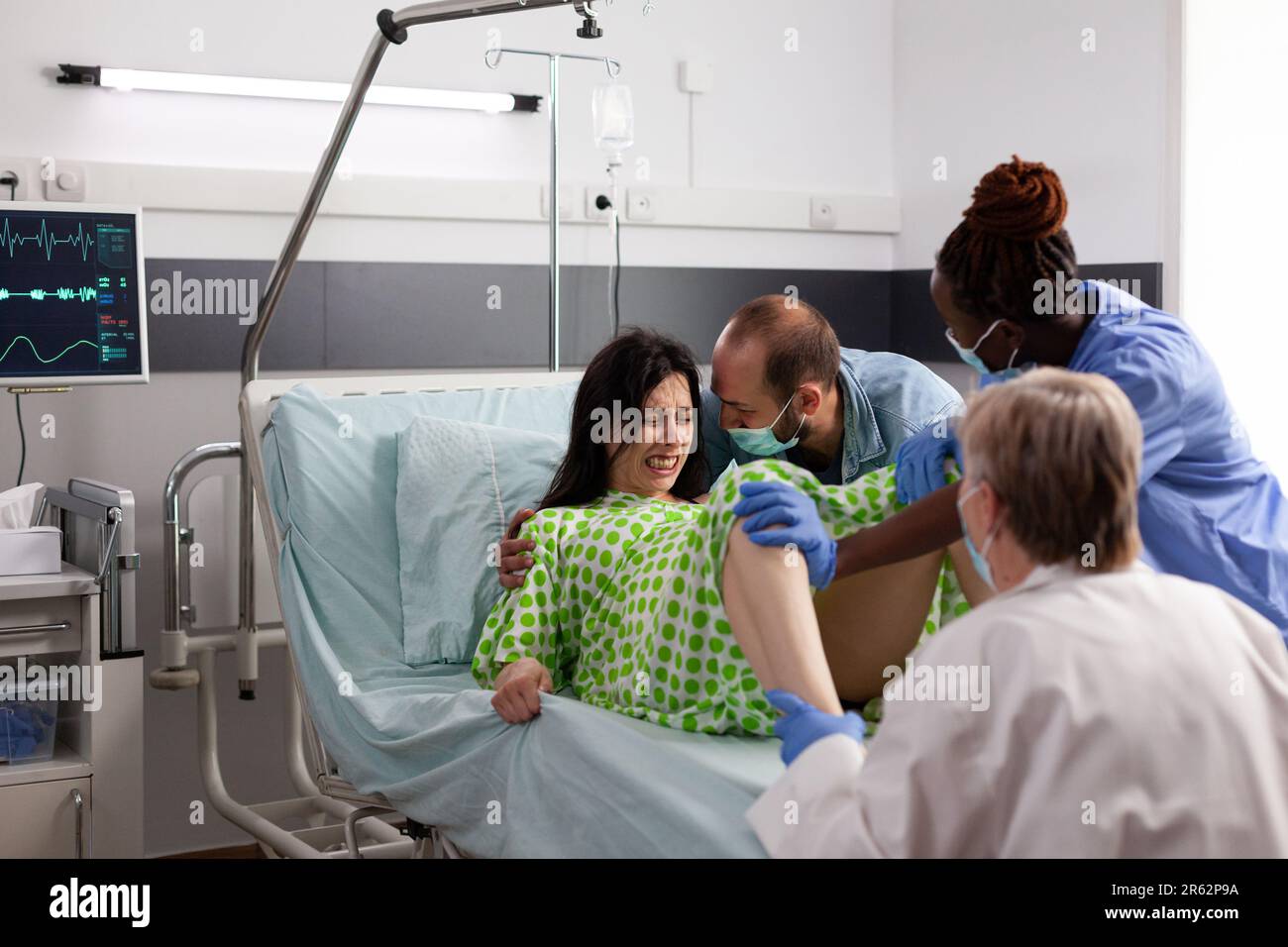 Diverse medical team delivering baby for woman with painful labor ...