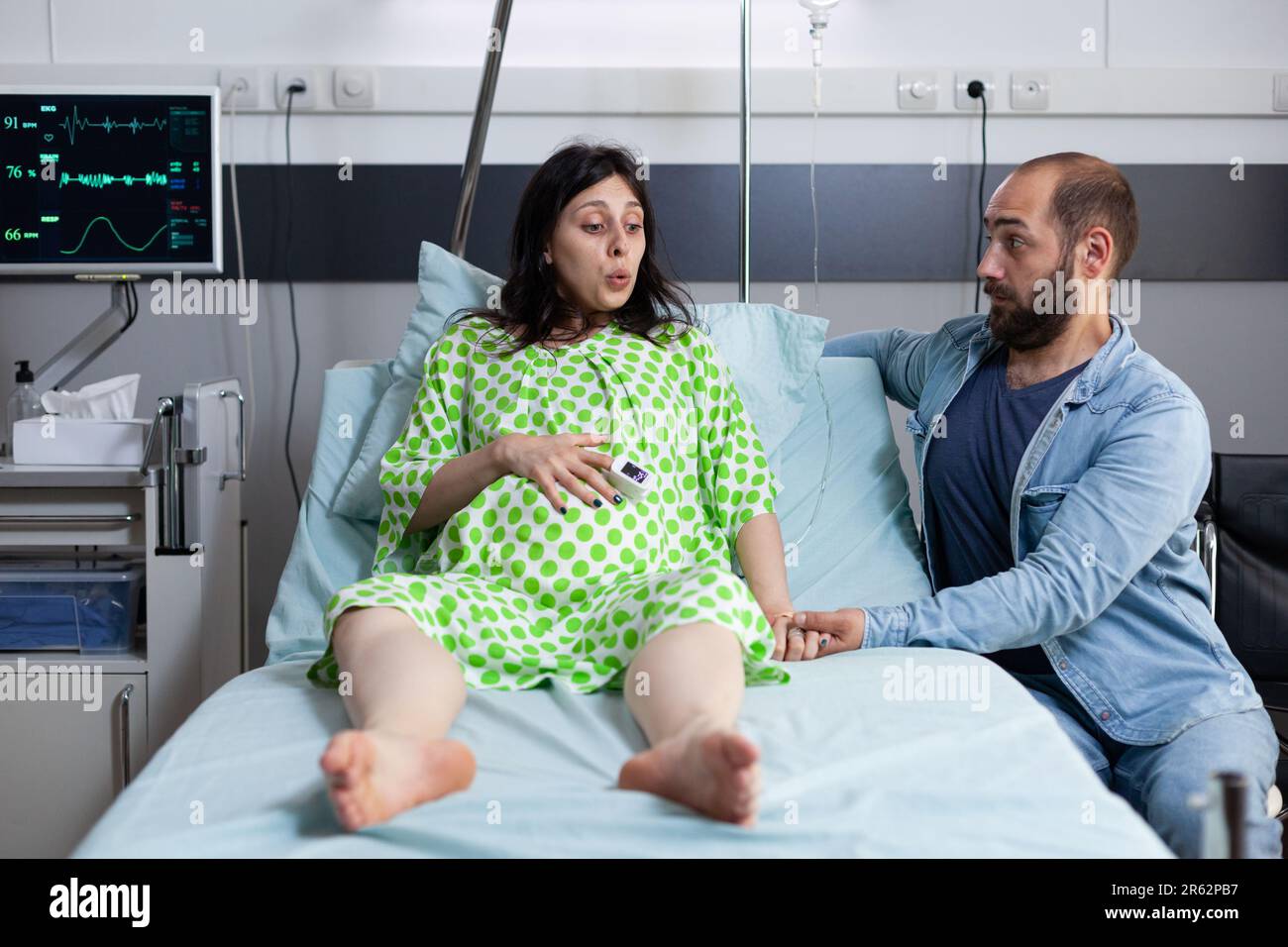 Pregnant patient sitting in hospital ward bed with husband beside her ...