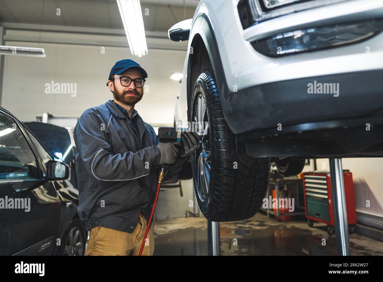 Auto mechanic standing by the car on a lift and replacing a wheel with ...