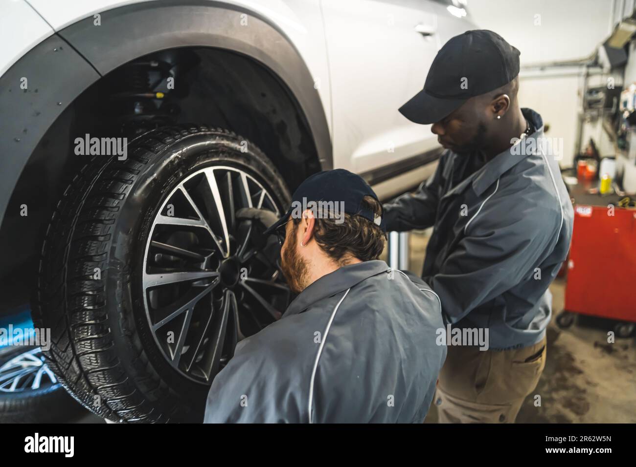 Two men car mechanics at work, changing a car wheel of a lifted vehicle ...
