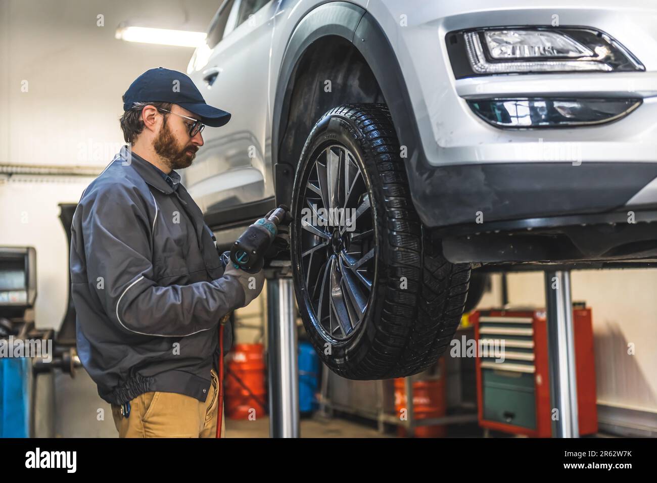 Car mechanic replacing wheel of a lifted vehicle with pneumatic wrench ...