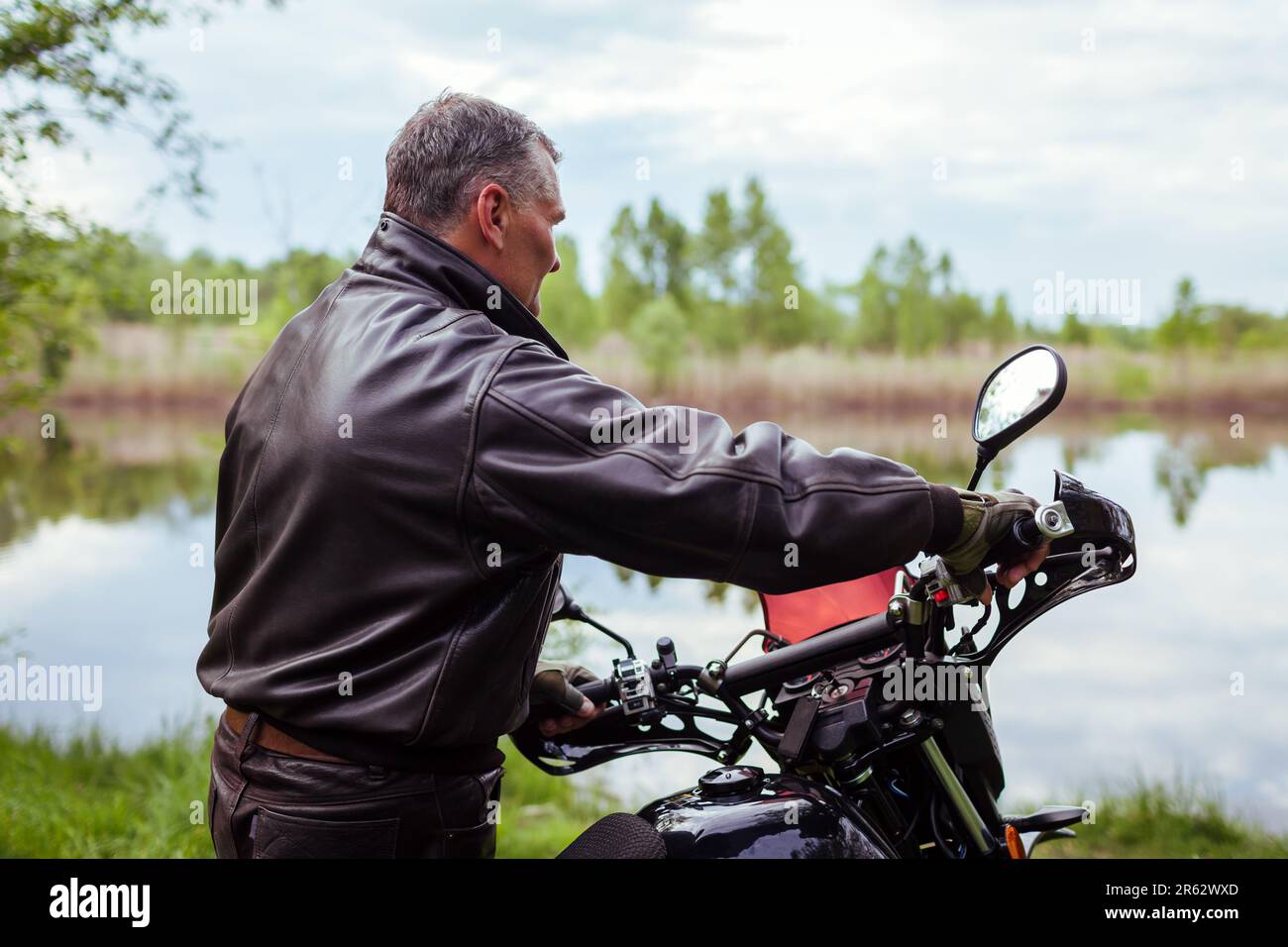 Back view of senior biker riding motobike outdoors. Man holding helm of ...