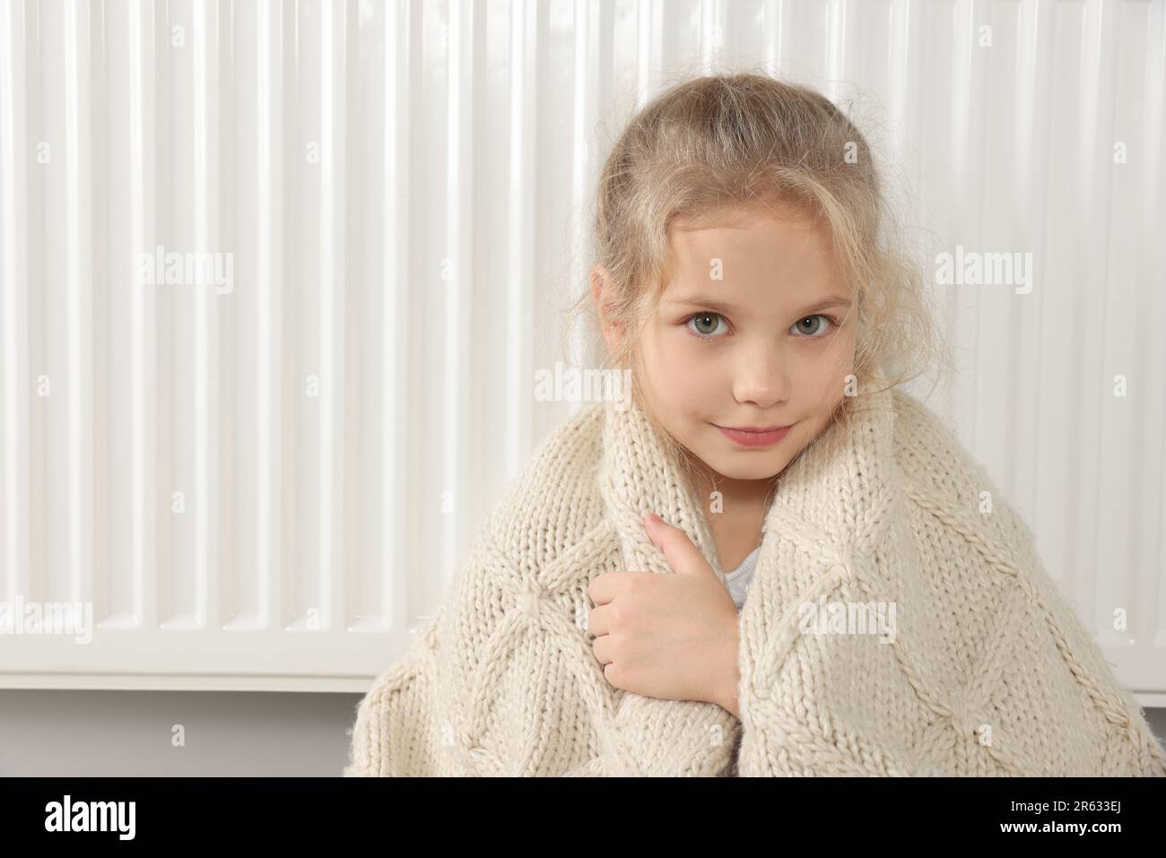 Little girl covered with knitted plaid sitting near heating radiator at ...