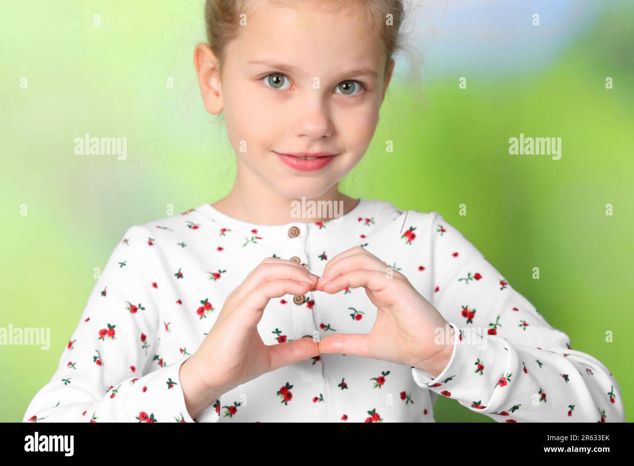 Cute little girl making heart with hands on blurred background, closeup ...