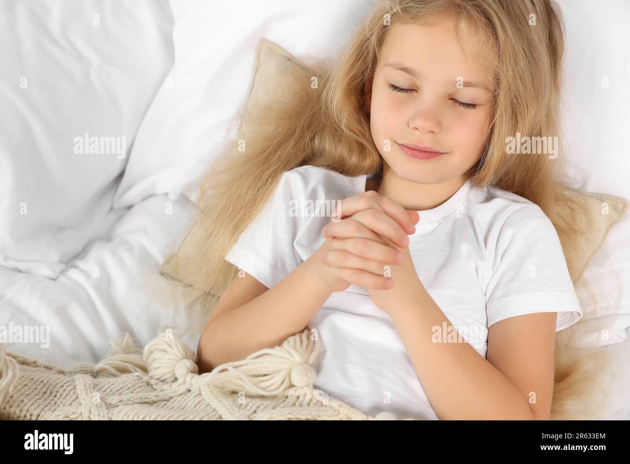 Girl with clasped hands praying in bed Stock Photo - Alamy