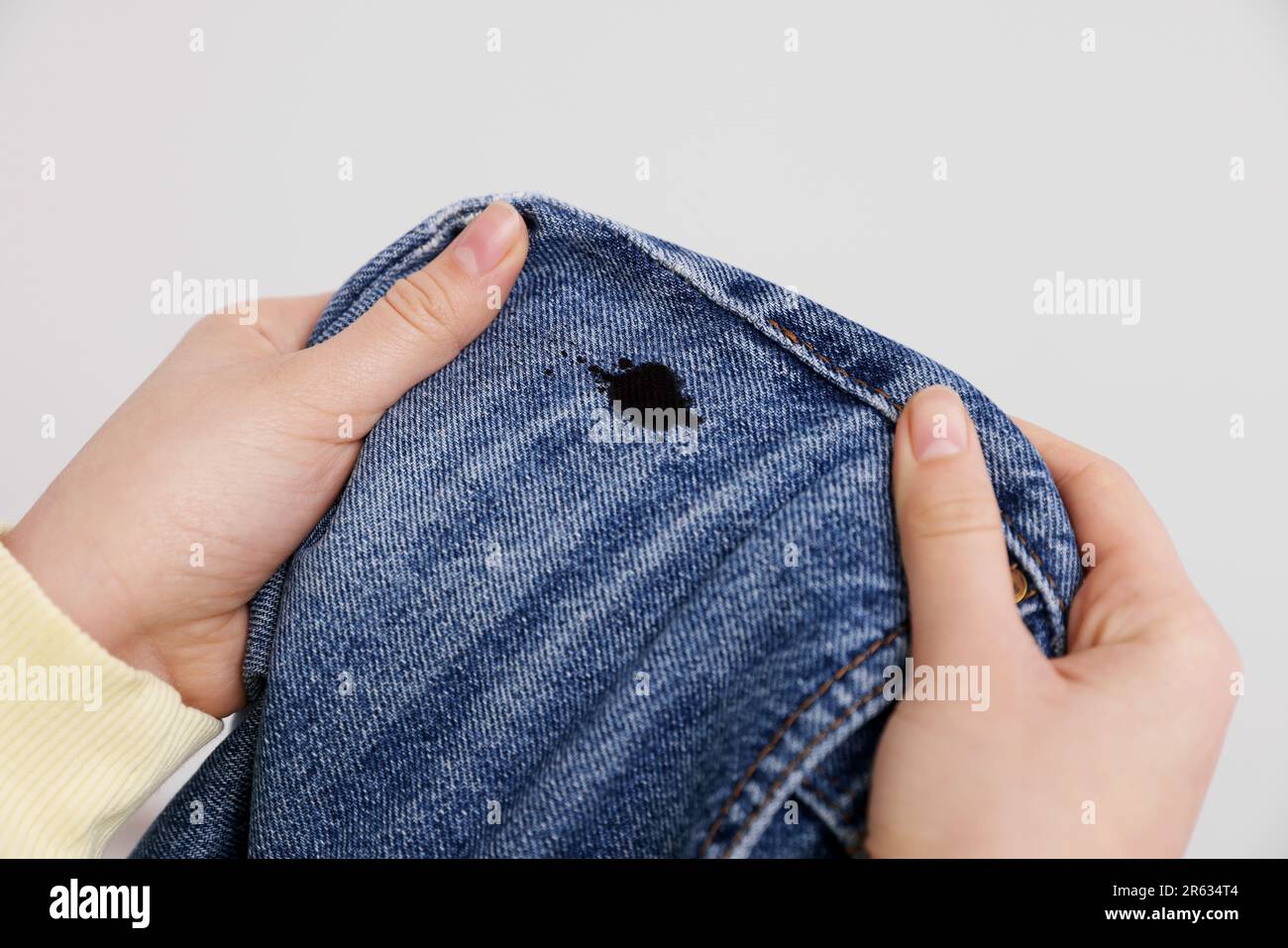 Woman holding jeans with black ink stain on light grey background ...