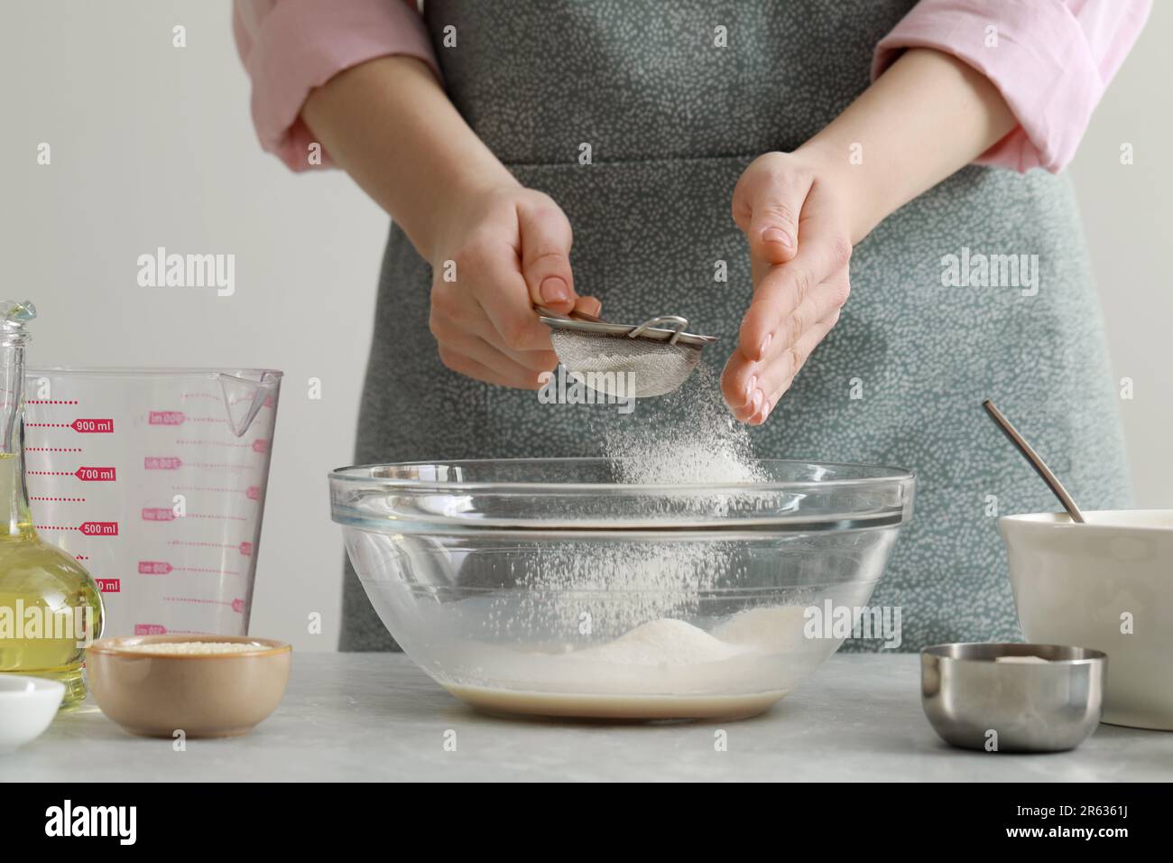 Woman sifting flour into bowl at grey marble table indoors, closeup ...