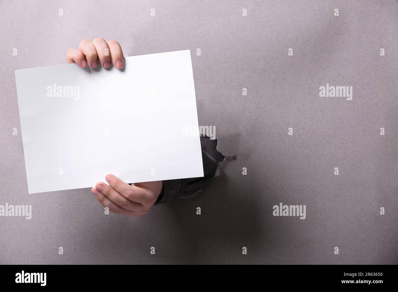 Man holding sheet of paper through hole in white paper, closeup. Mockup ...
