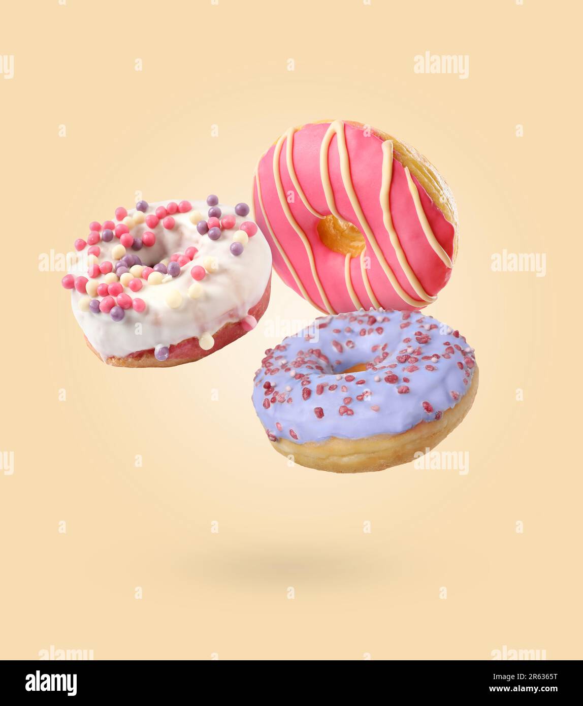Sweet tasty donuts falling on beige background Stock Photo - Alamy