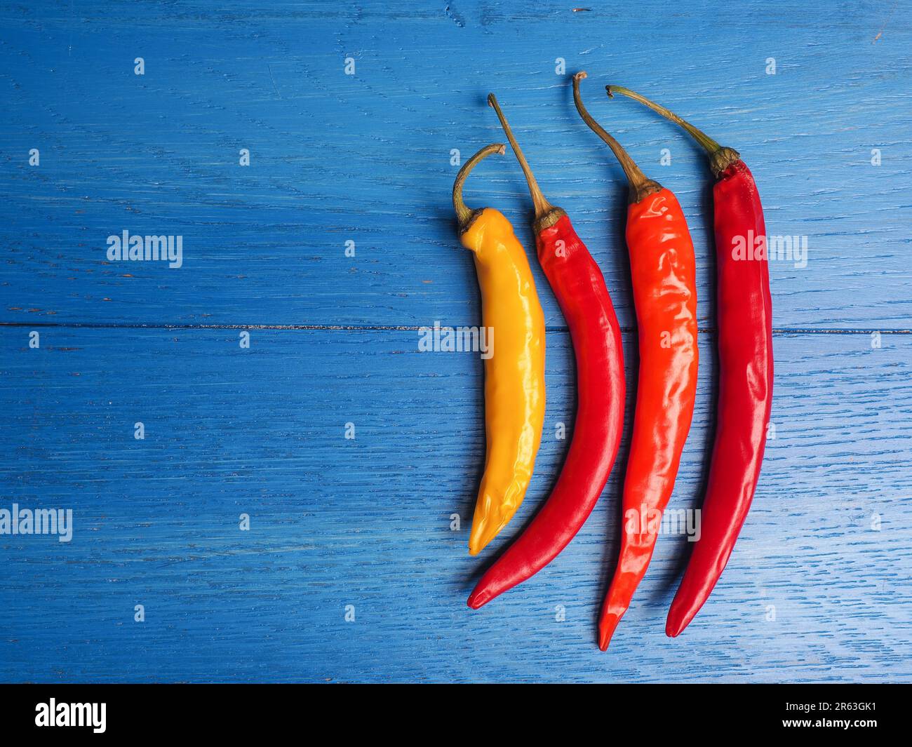 Four hot chilies on a rustic blue wooden background Stock Photo - Alamy