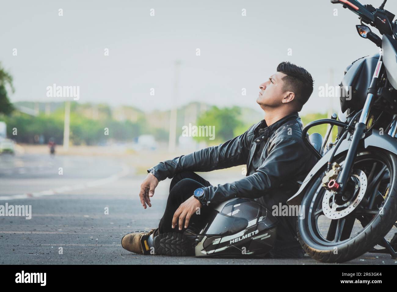 Male motorcyclist sitting and leaning on his motorcycle on the asphalt ...