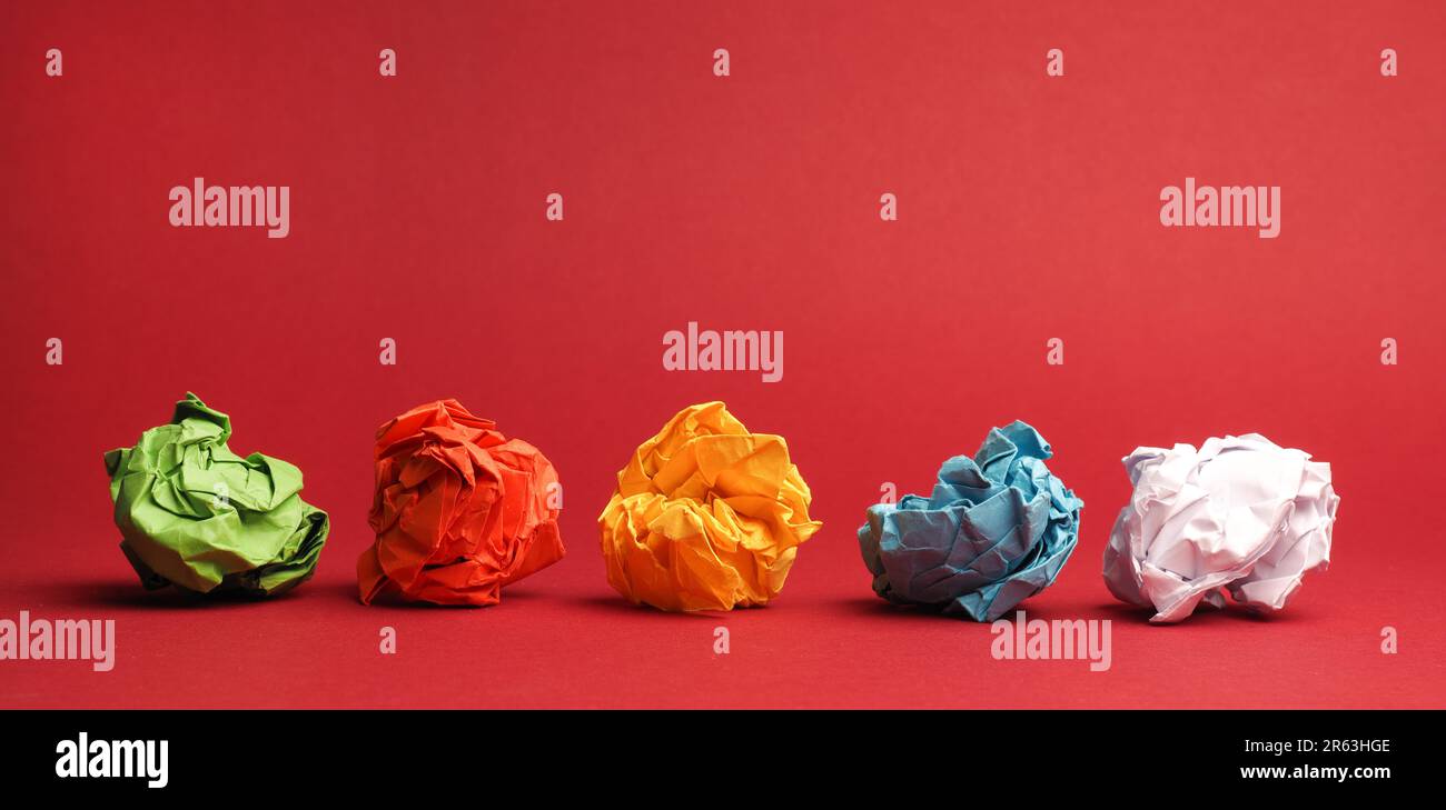 Colorful crumpled paper balls on a red studio background, creativity or ...