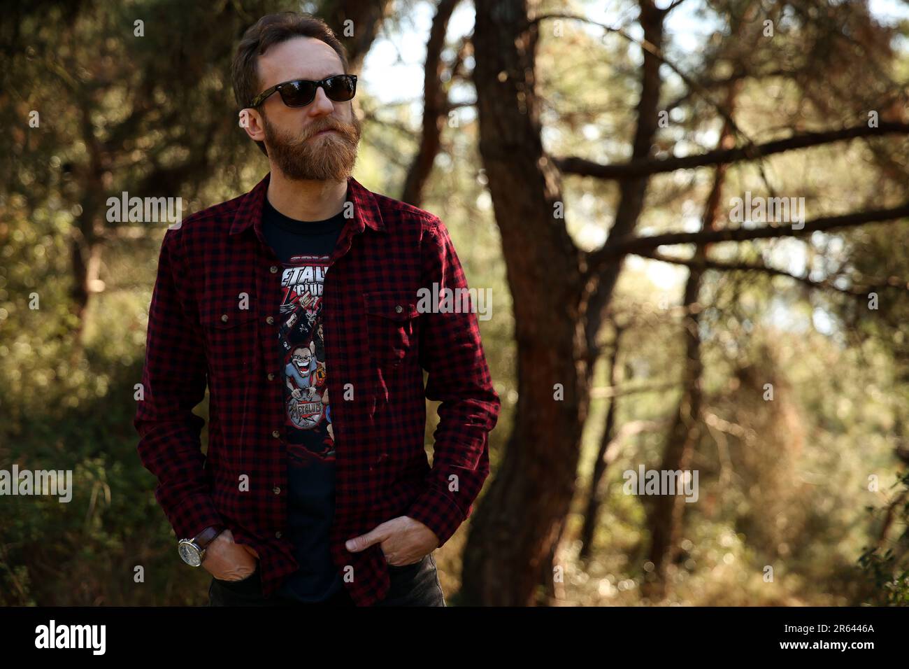 Bearded man with sunglasses and a red shirt posing in front of a blurry ...