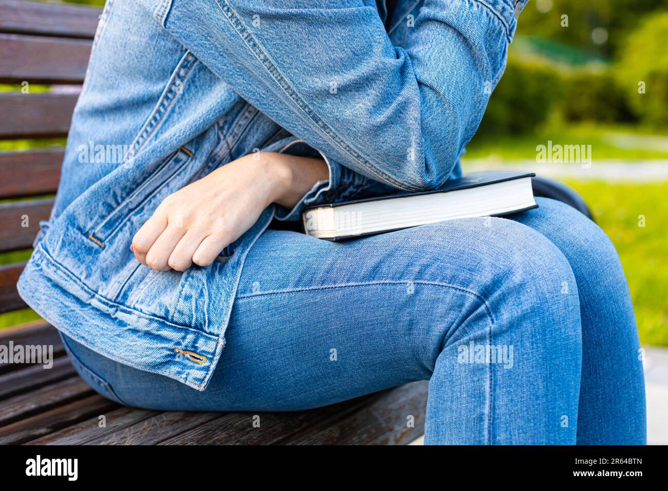 girl sitting on a bench with a book on her lap. girl reading a book in ...