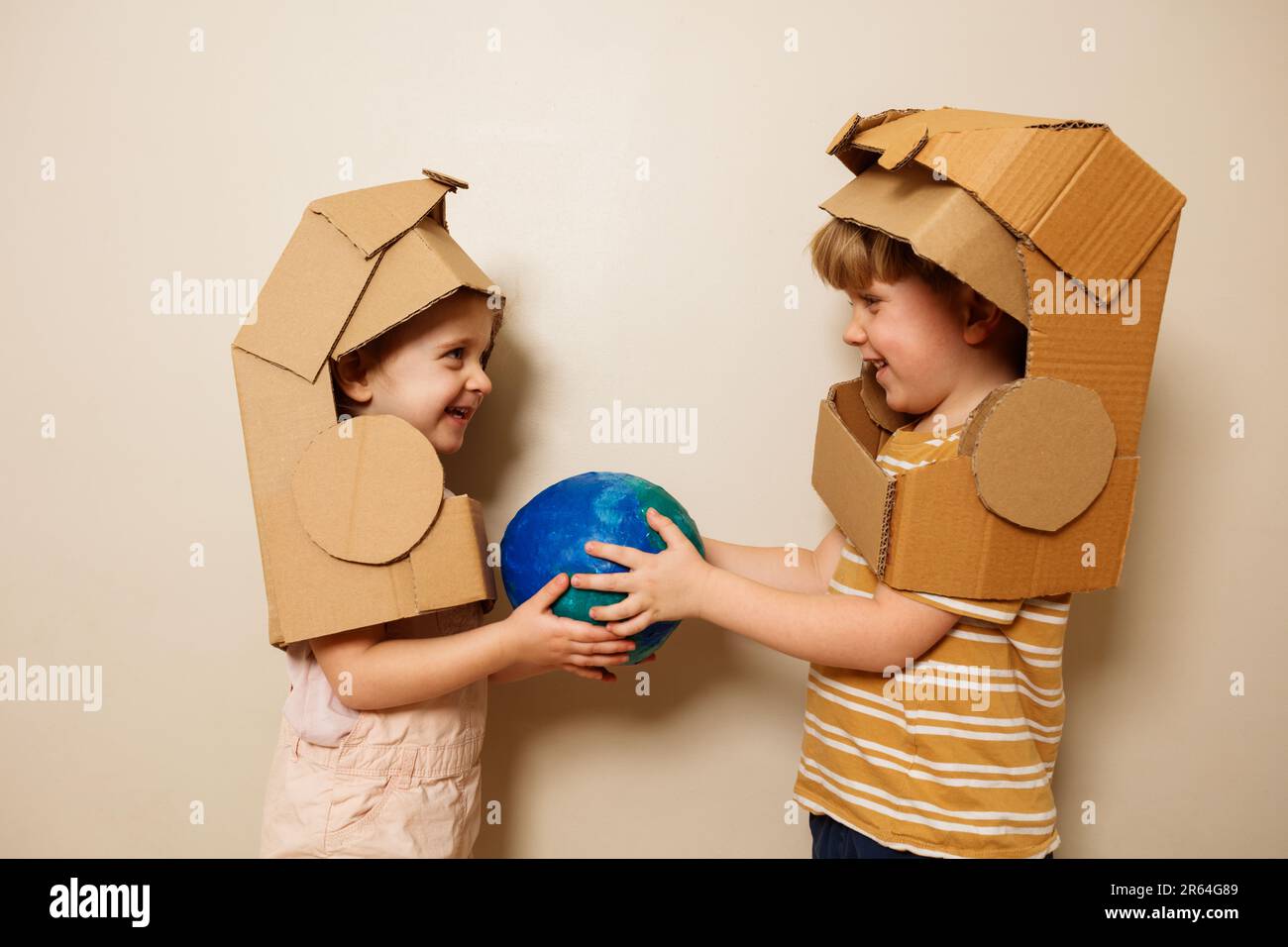 Two kids smile holding a globe in cardboard astronaut helmets Stock ...