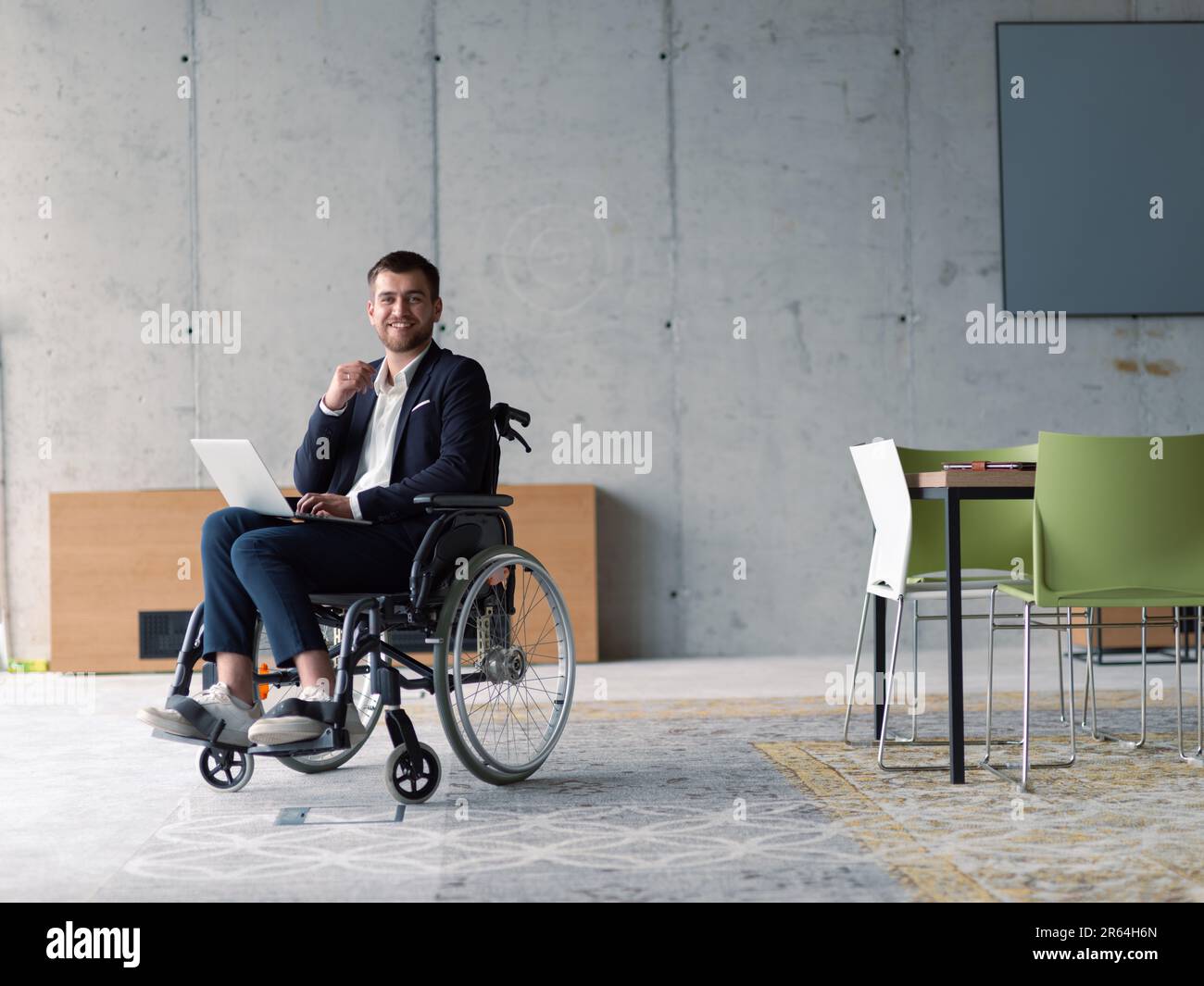 A businessman with disability in a wheelchair using laptop in a modern ...