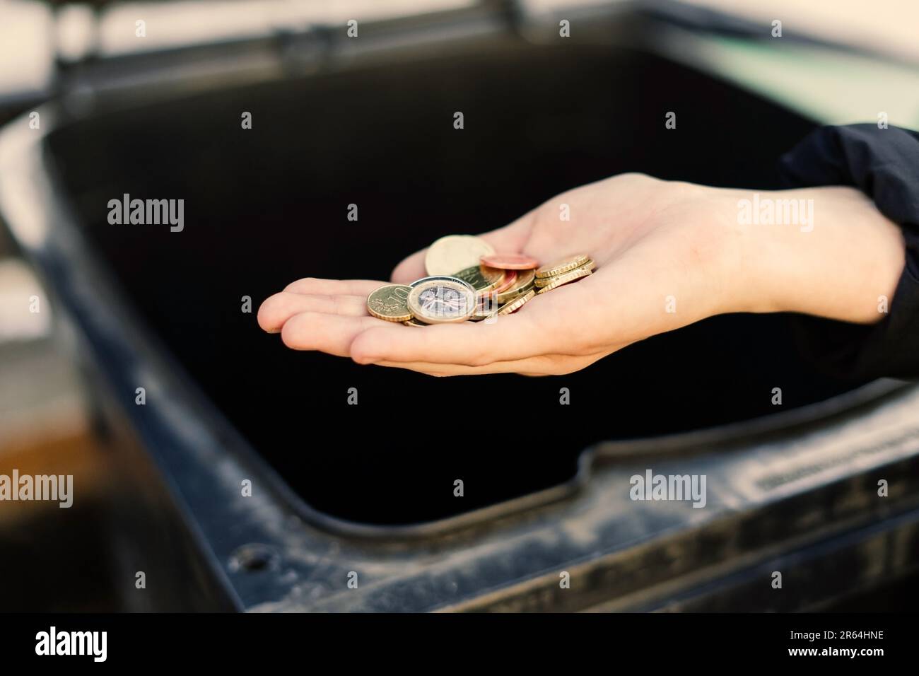 A kid girl hand throws a euro coins into a trash can dumpster, street ...