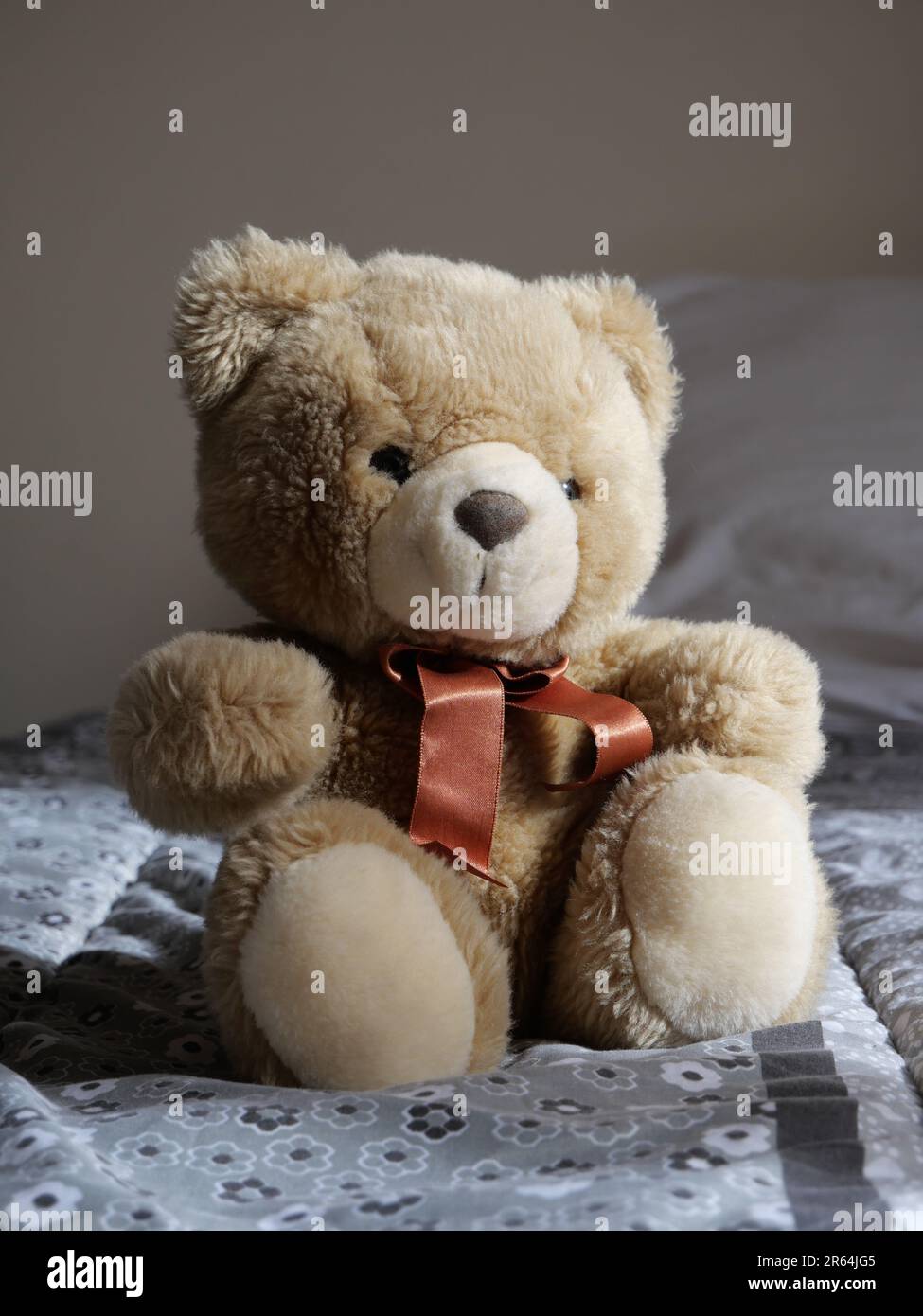A cozy brown plush teddy bear resting on a bed next to a white pillow ...