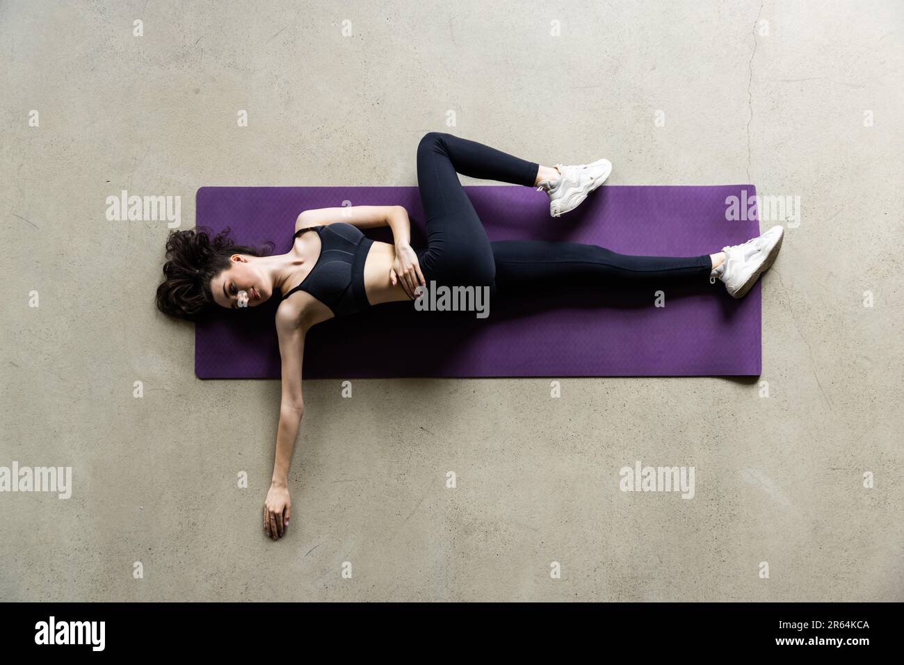 Sporty young woman lying on yoga mat doing sit-ups in gym. Top view of ...