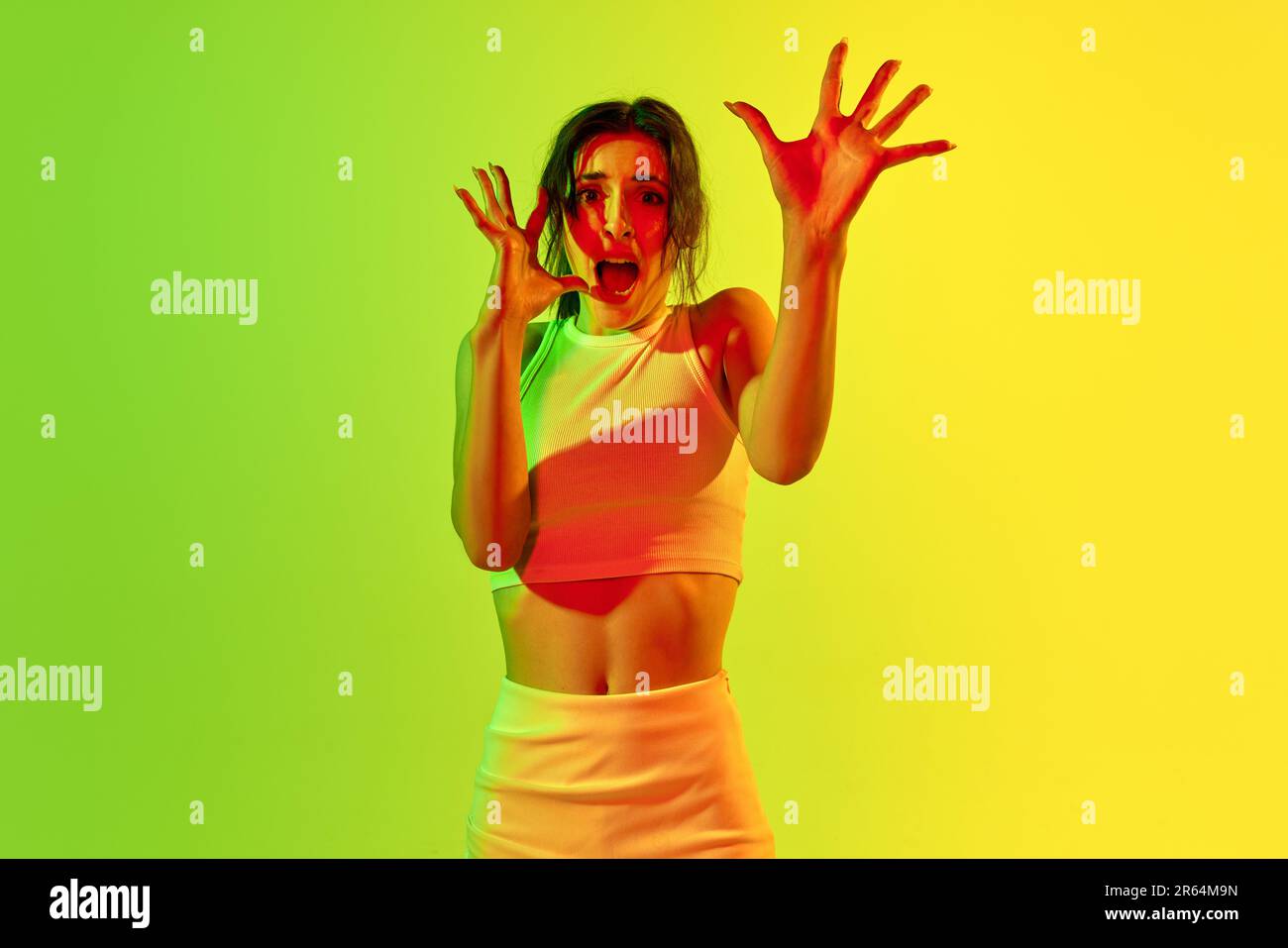 Portrait of frightened, young woman holding hands up with open mouth ...