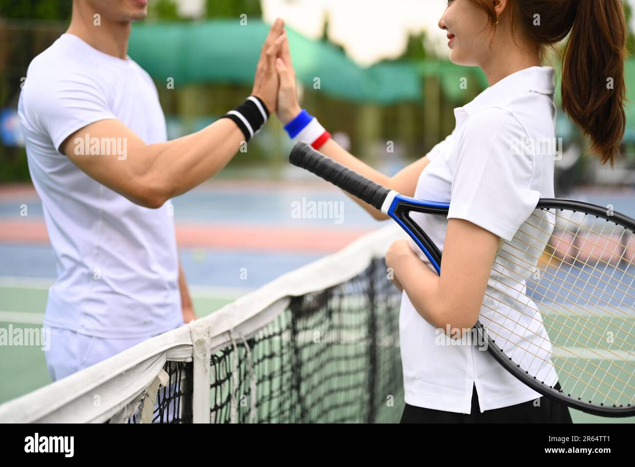 Shot of two young tennis players giving each other high five over net ...