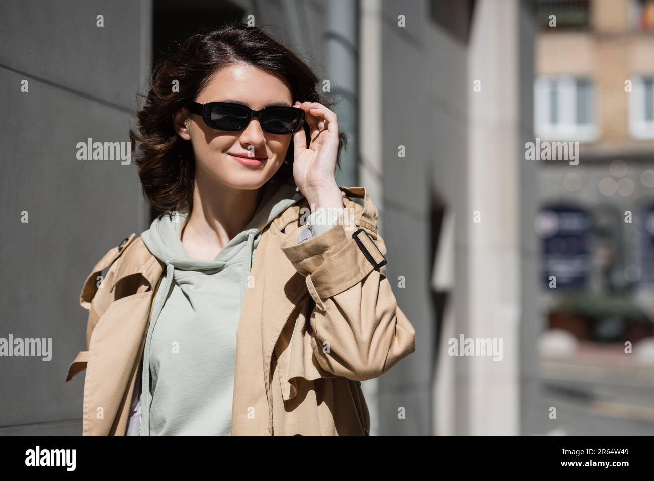 young and pleased woman with wavy brunette hair, in grey hoodie and ...