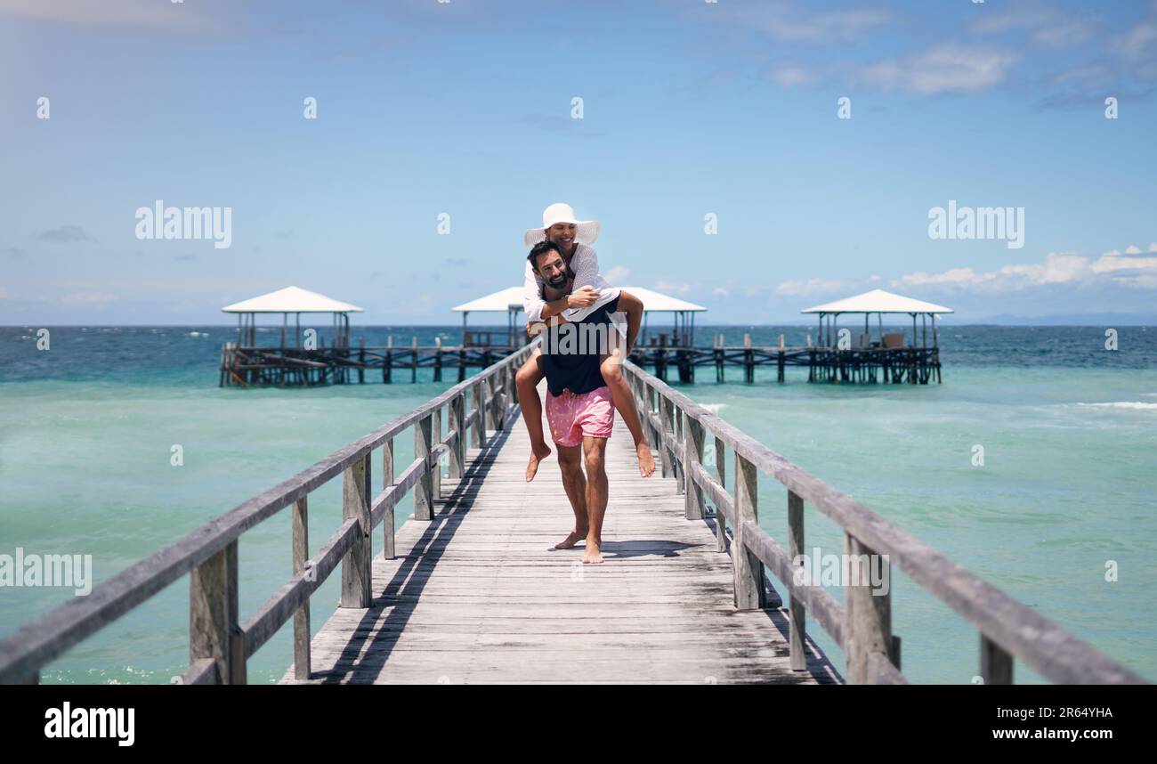 Couple, piggyback and outdoor beach deck on a tropical island with love ...