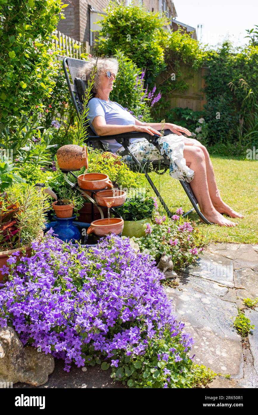 Woman relaxing on a sun lounger chair in a small urban garden with a ...