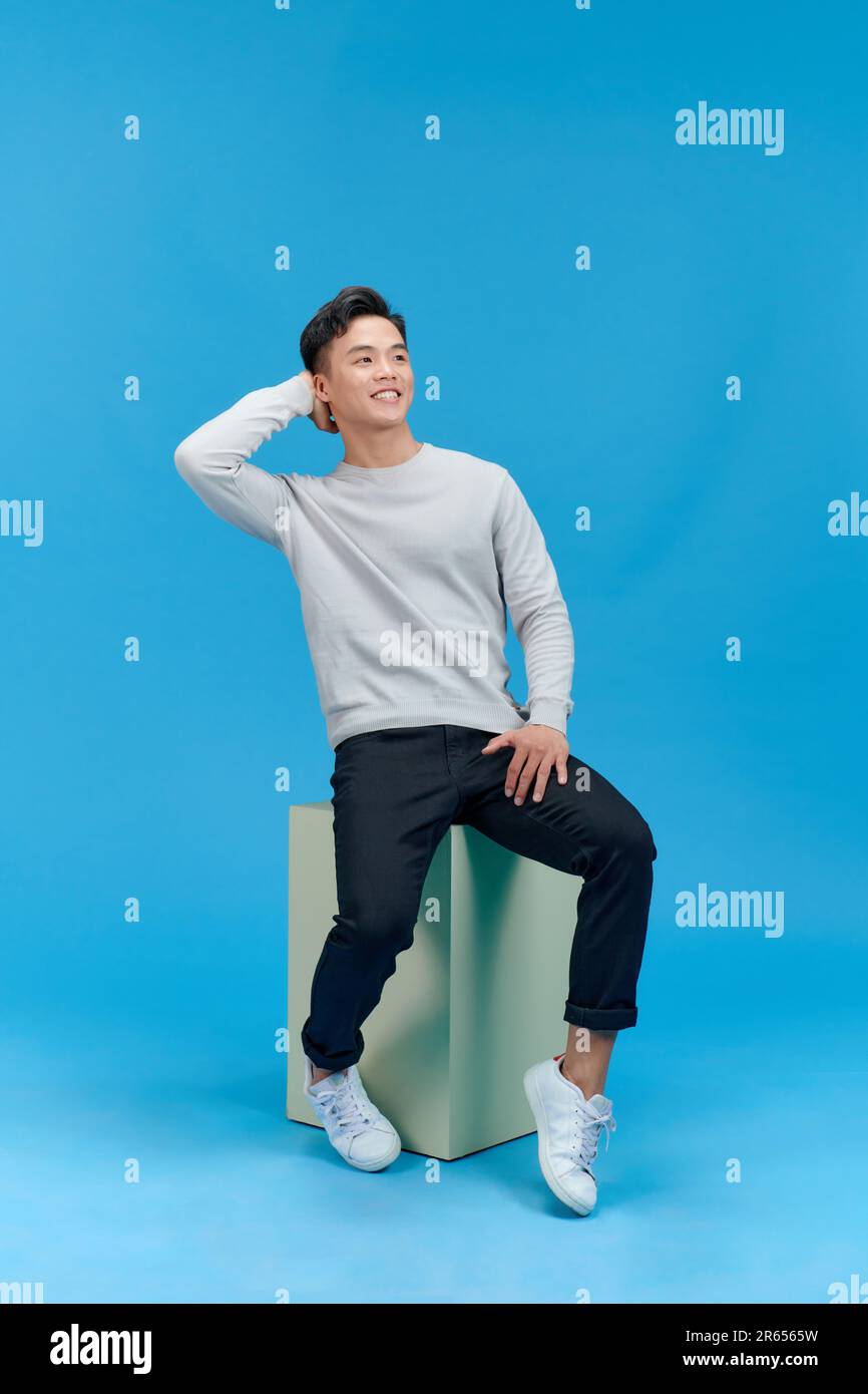 Casual young man sitting on a mint column isolated on blue background ...