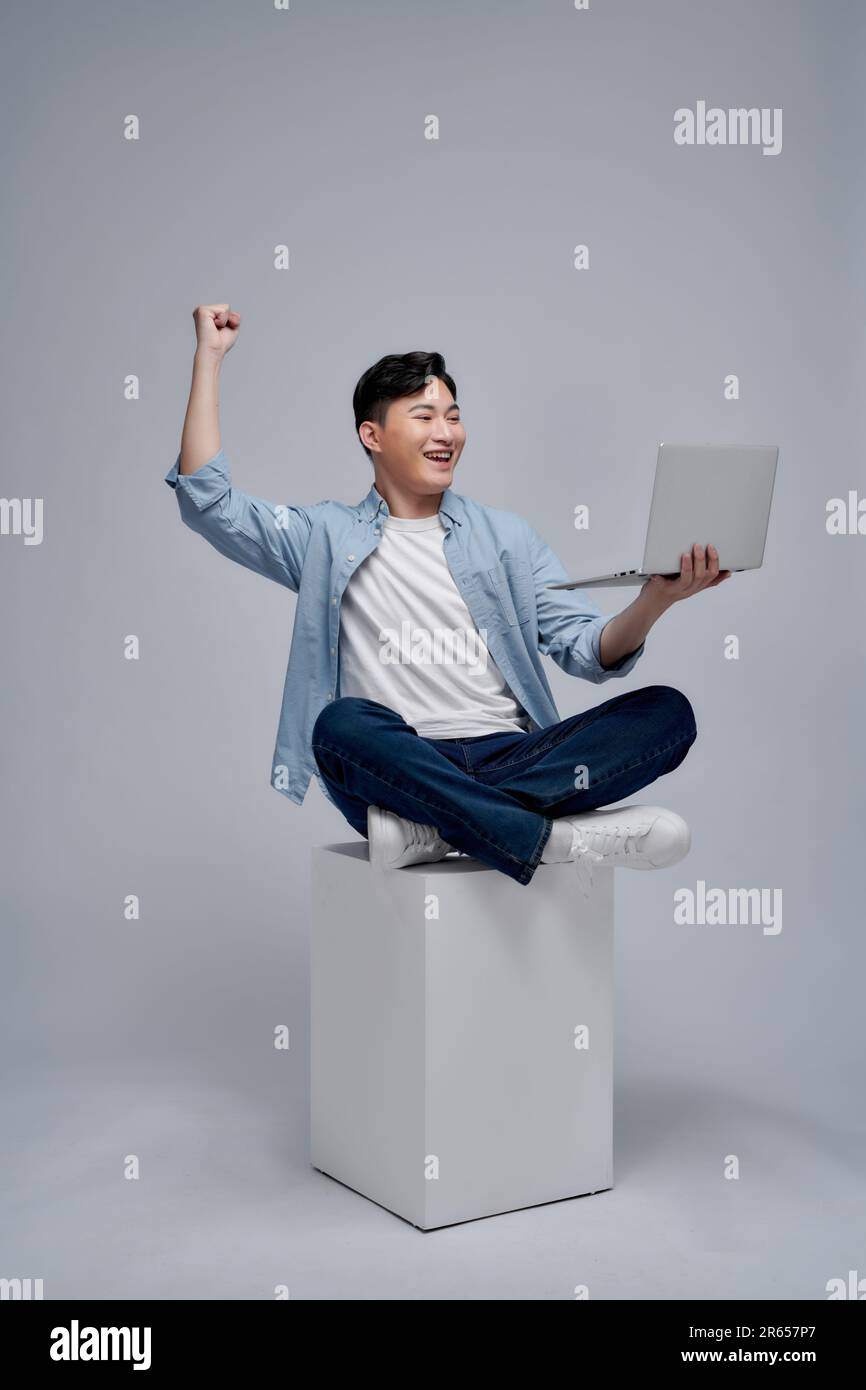 Full length photo of young excited funny guy fists up sitting platform ...