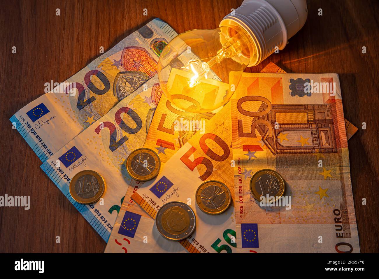 Light bulb lit, with coins and banknotes next to it. Rising electricity ...