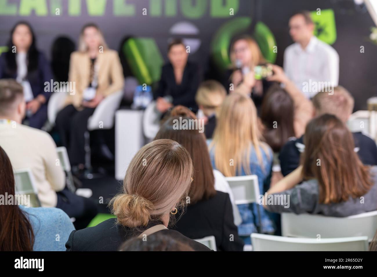 Back view of women and men sitting in front of stage with row of ...