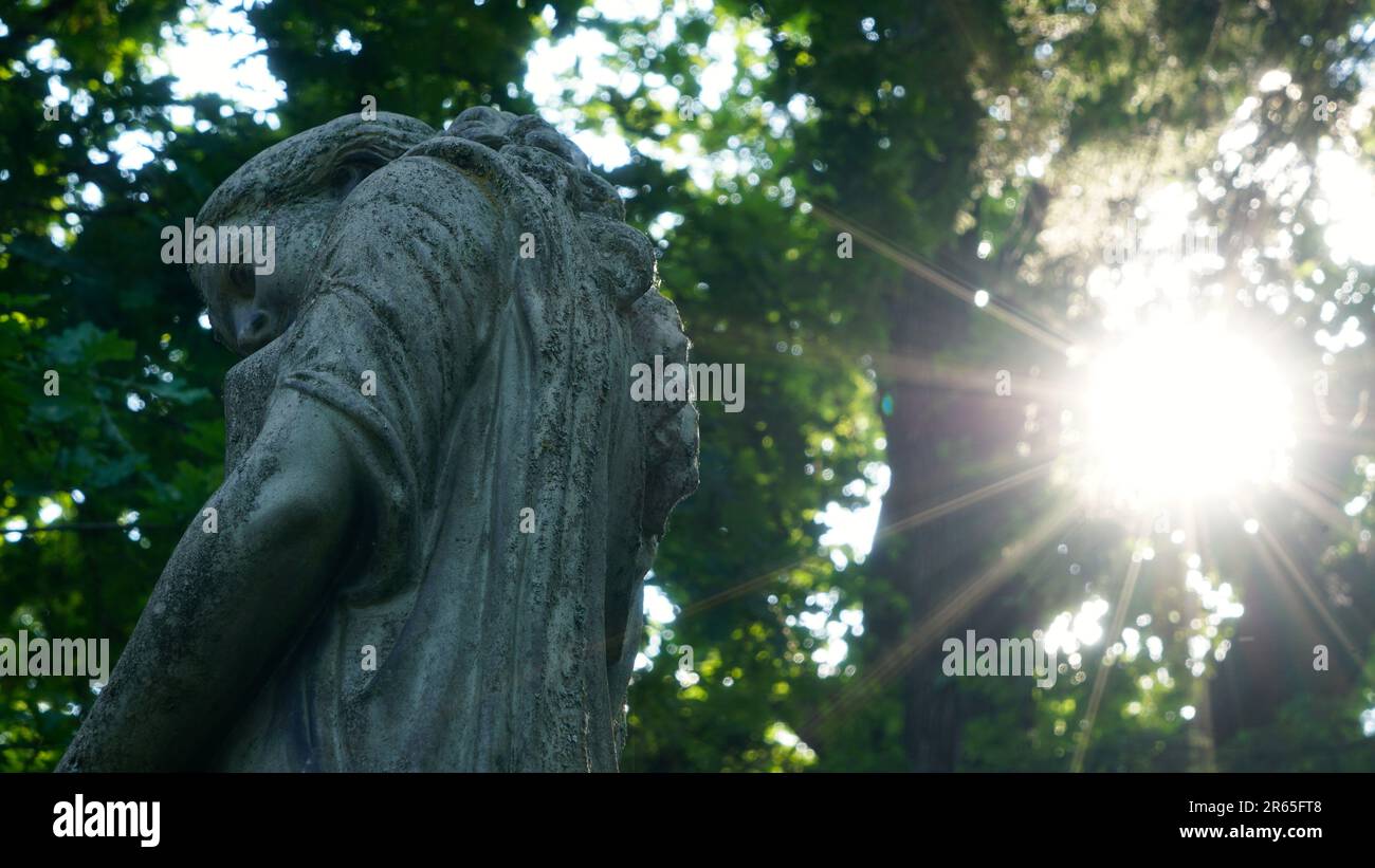 Sculpture of a beautiful woman in a graveyard / cemetery. Sunrays ...