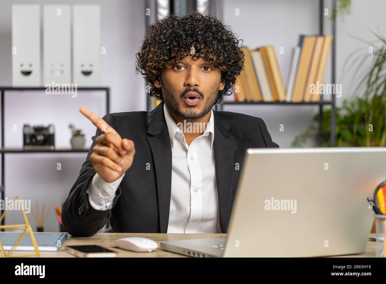 Indian young businessman working on laptop computer shakes finger and ...