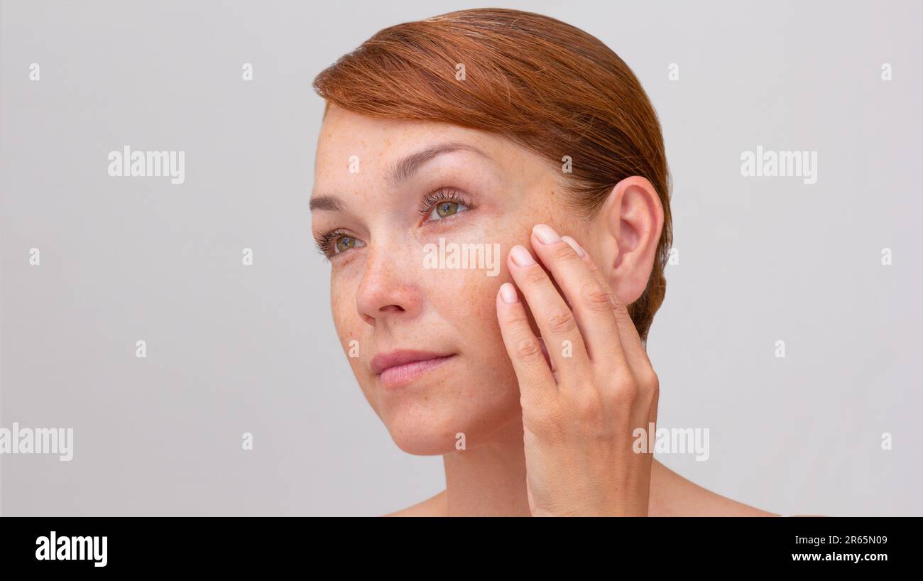 Portrait of cropped caucasian middle aged woman face with freckles touching skin by hand on ...