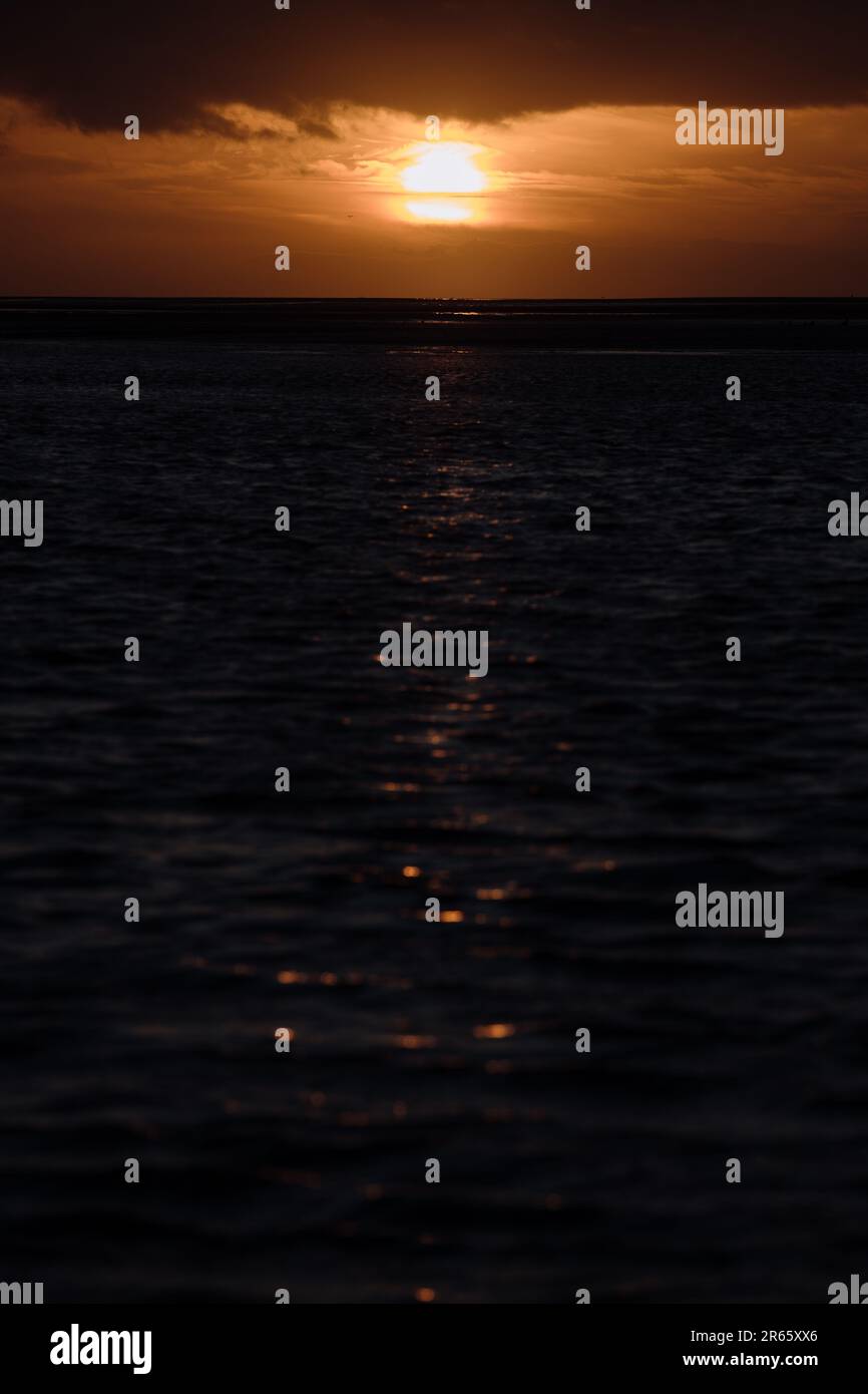 A vibrant orange sunset casts a warm glow over the horizon of an ocean ...