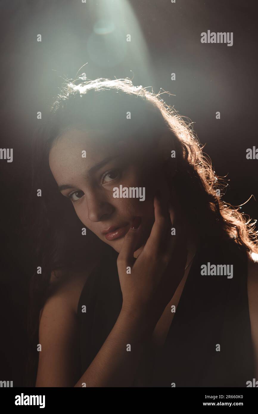 A young female in a dimly lit setting, standing against a dark backdrop ...