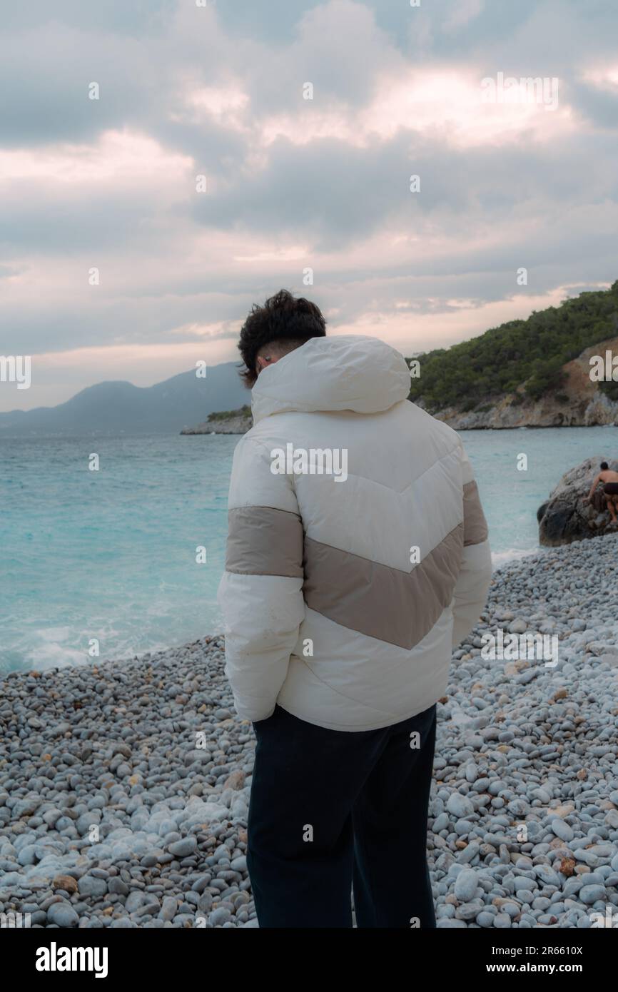 A man stands on a rocky shoreline, gazing out at the sea before him ...