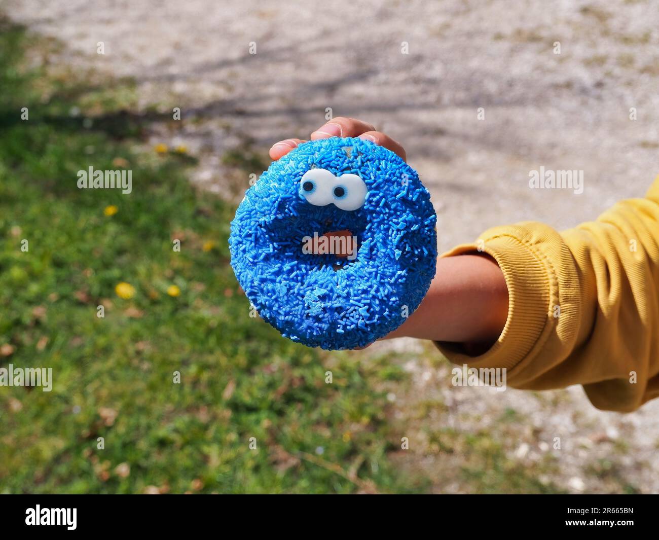A closeup of a human hand holding a blue doughnut with a cartoon face ...