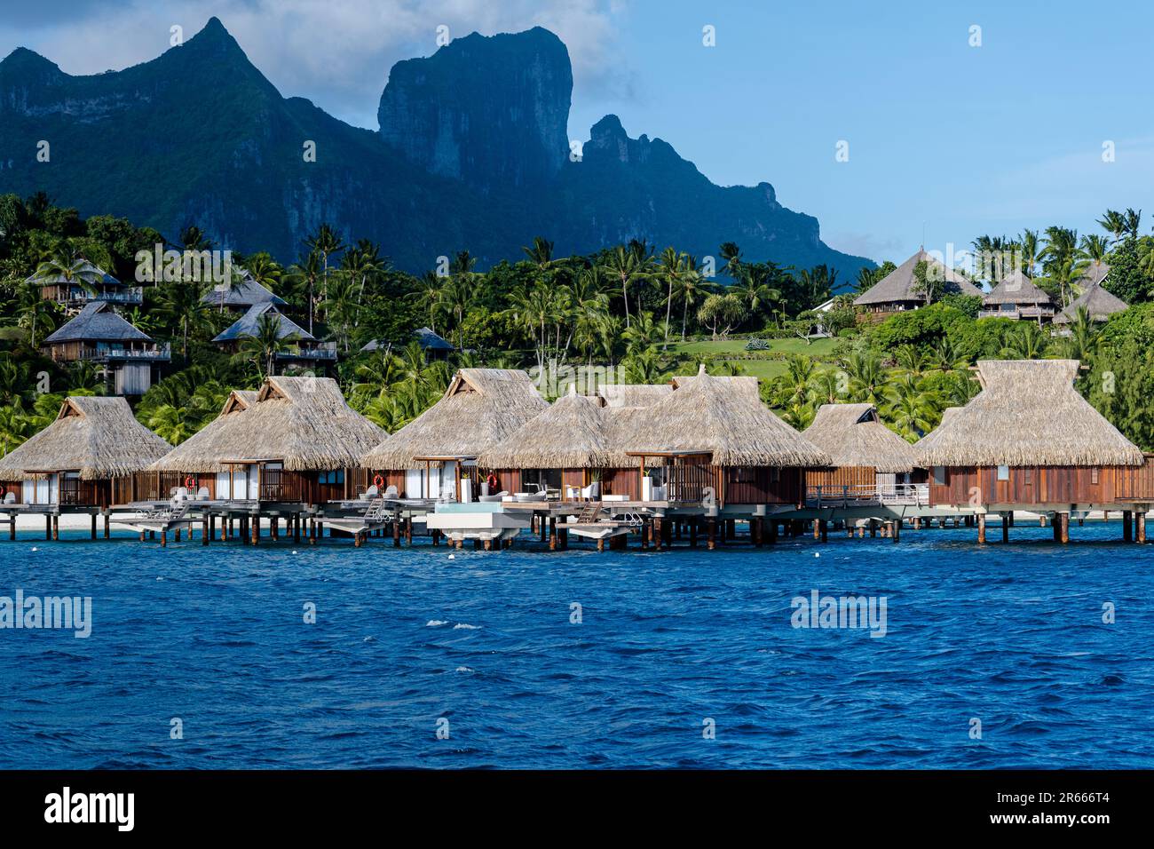 Thatched huts on stilts over water and on land with mountains in the ...