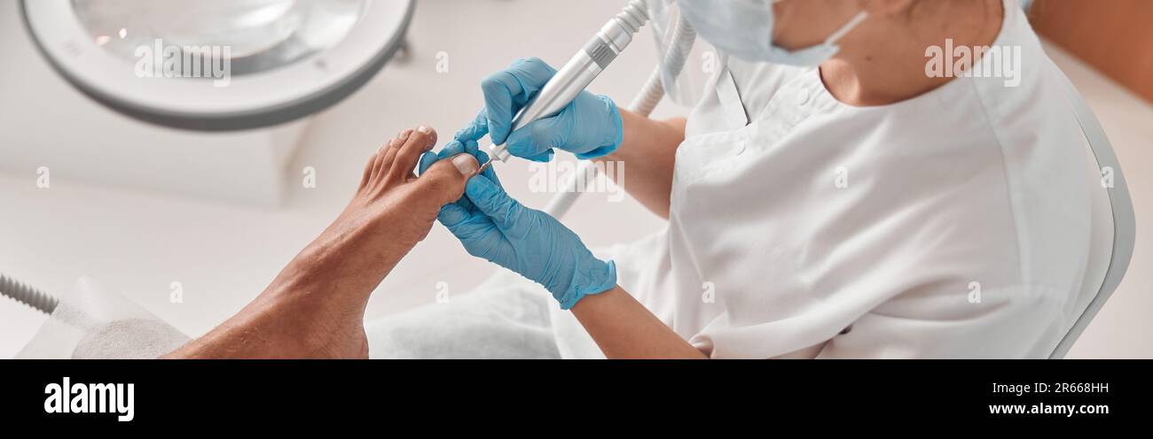 Lady uses grinding machine to polish toenail of male client at in ...