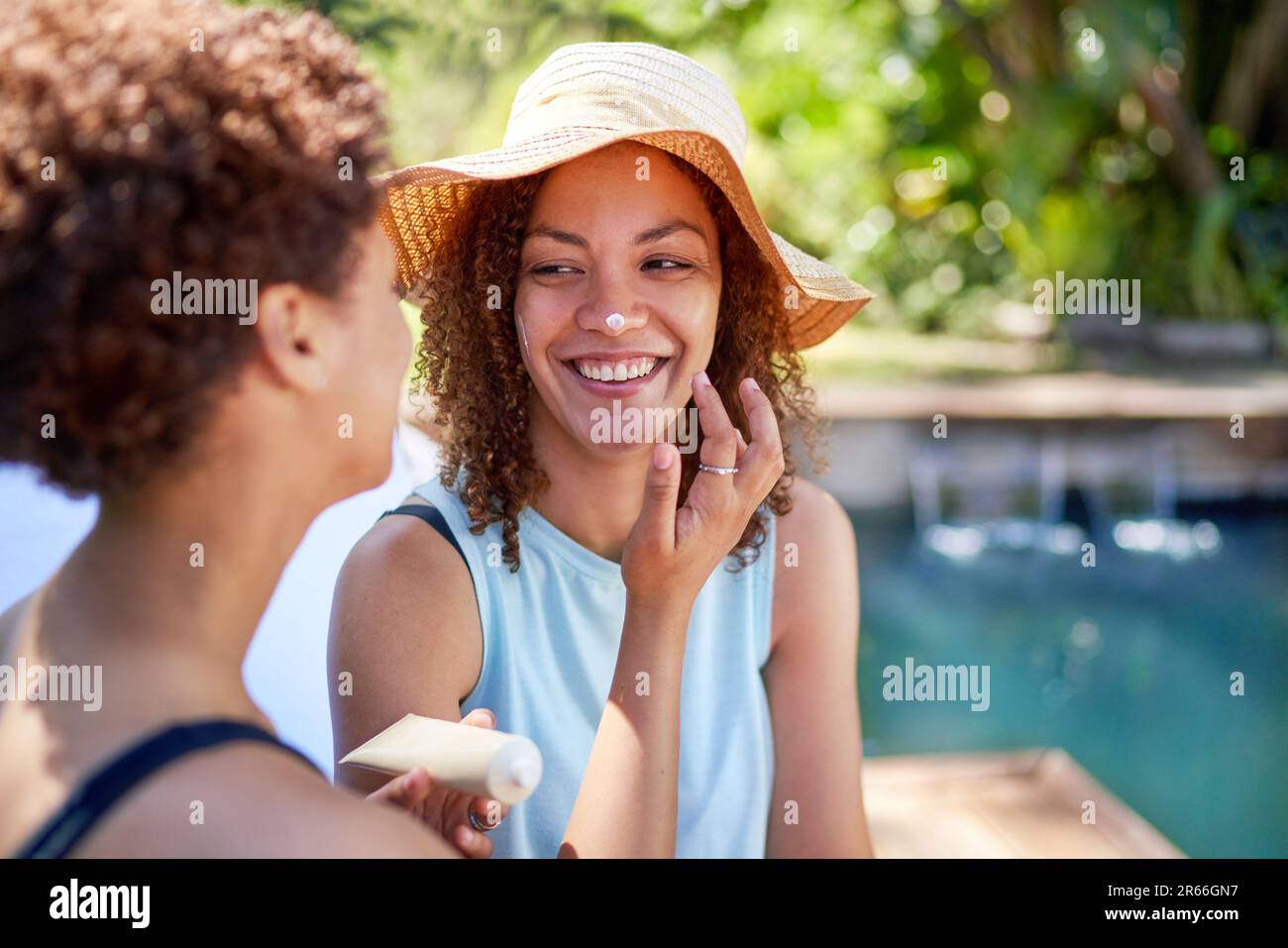 Happy, playful lesbian couple applying sunscreen to nose at poolside ...