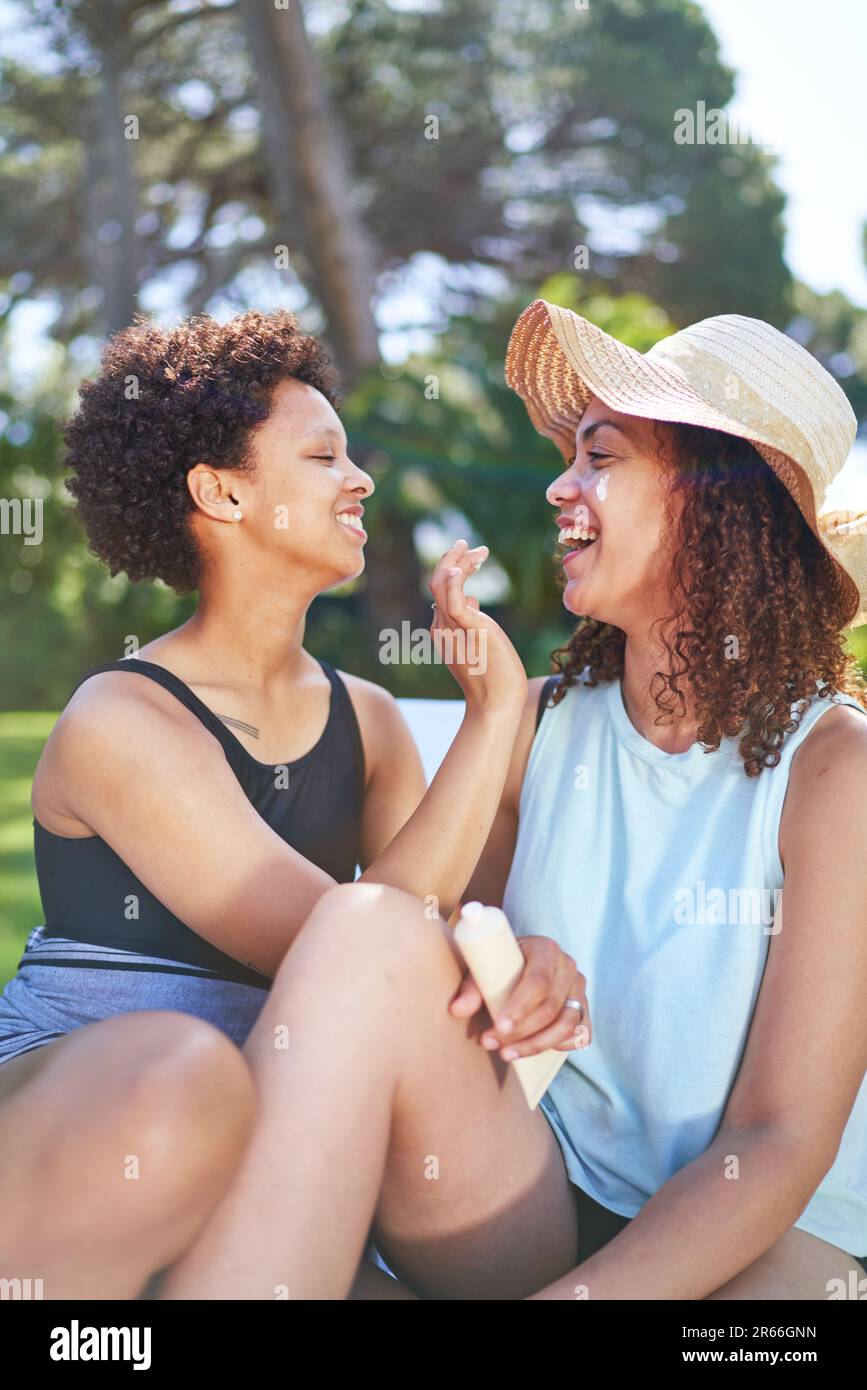 Happy lesbian couple applying sunscreen to face in summer backyard ...