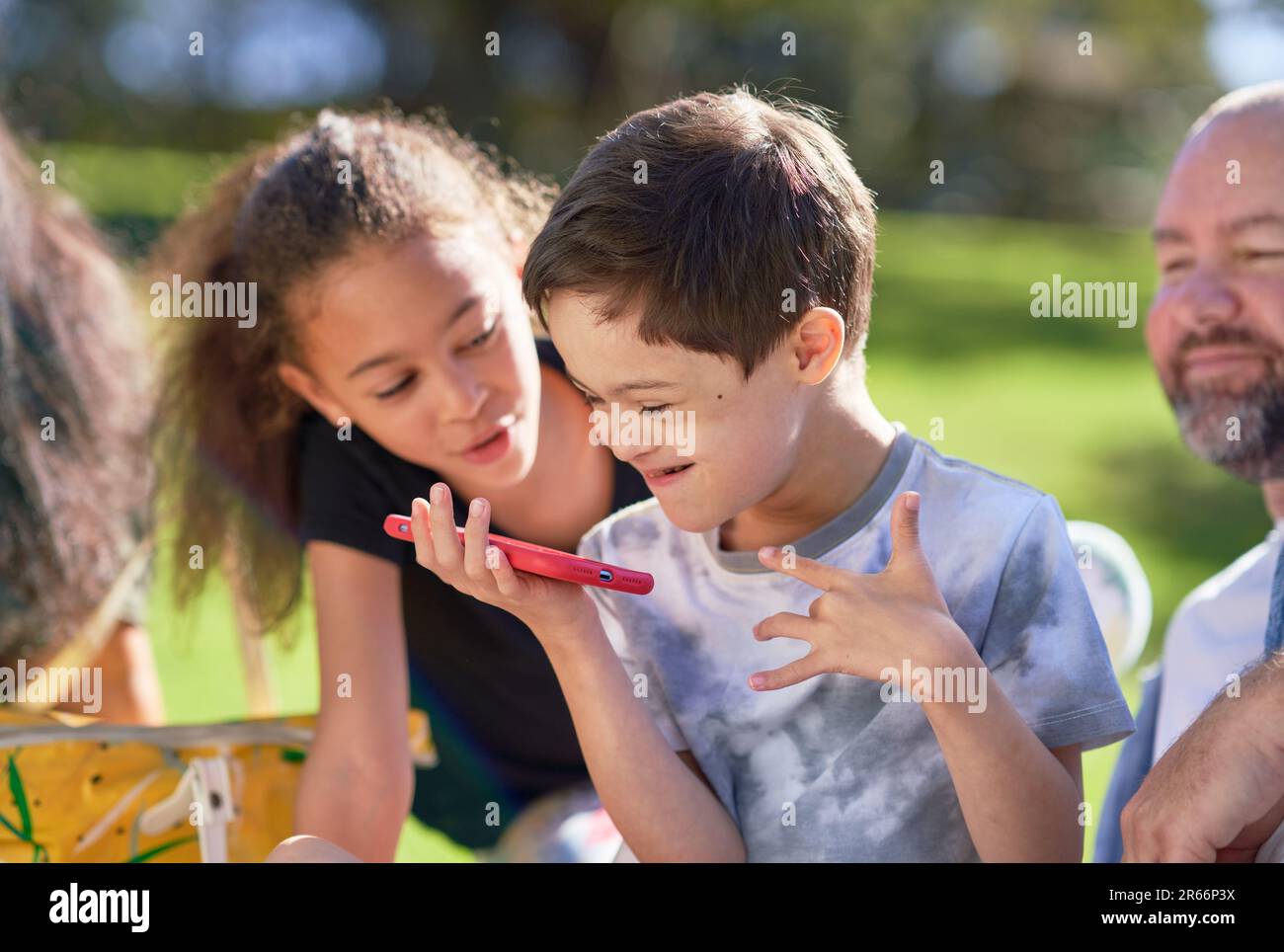 Sister watching brother with Down Syndrome using smart phone in park ...